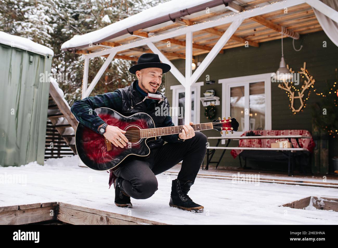 Radiant musician in a hat and leather jacket crouching with guitar in ...