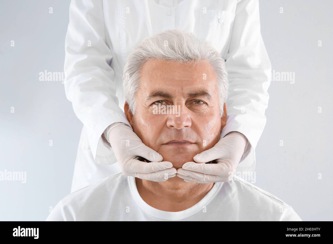 Doctor examining senior man face before cosmetic surgery on white ...