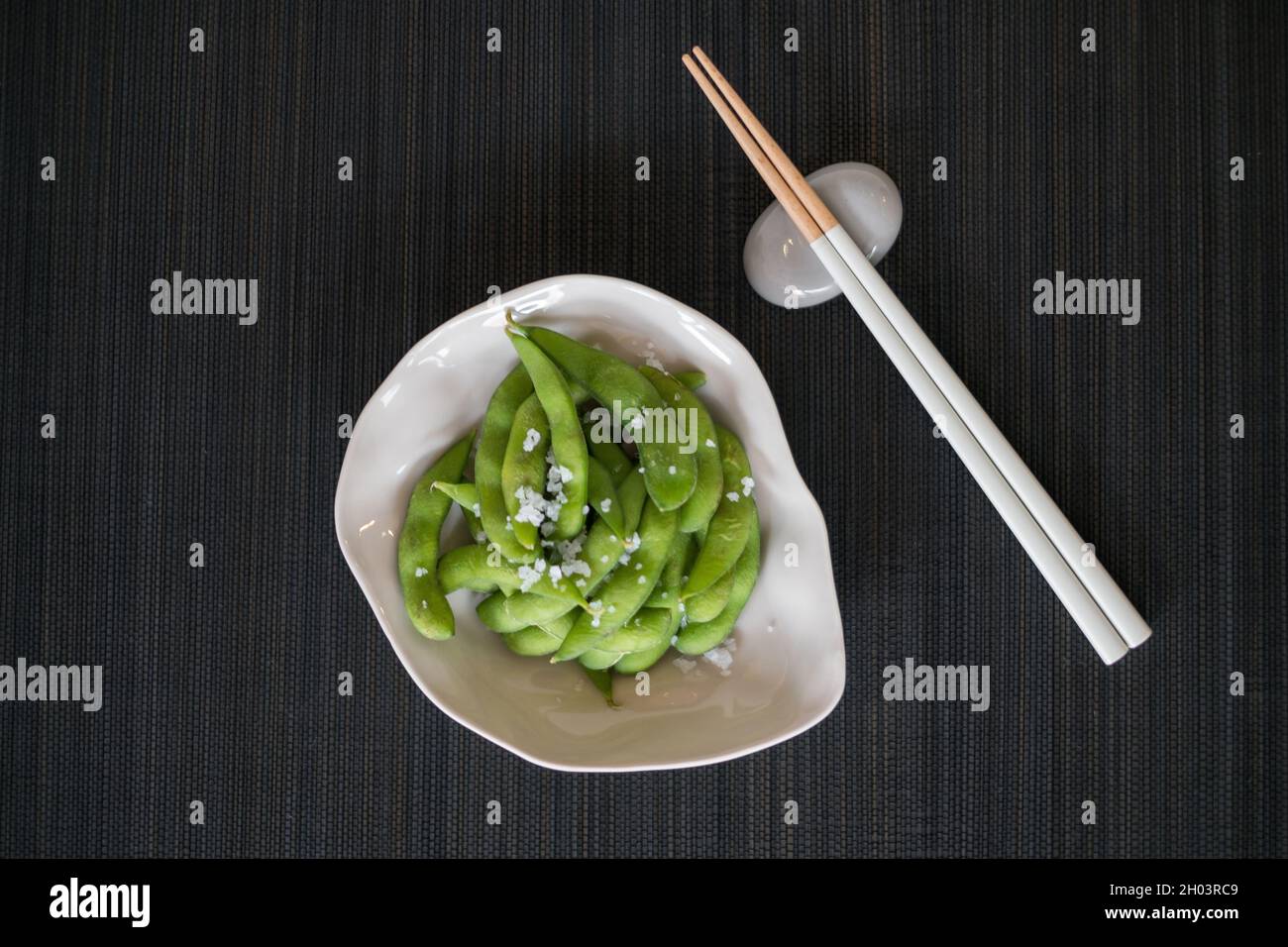Green pea pods on white plate with wooden chopsticks on black mat in ...