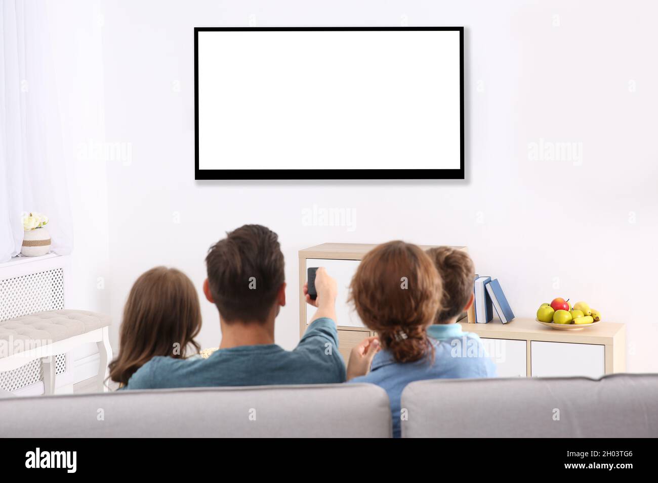 Family with remote control sitting on couch and watching TV at home ...