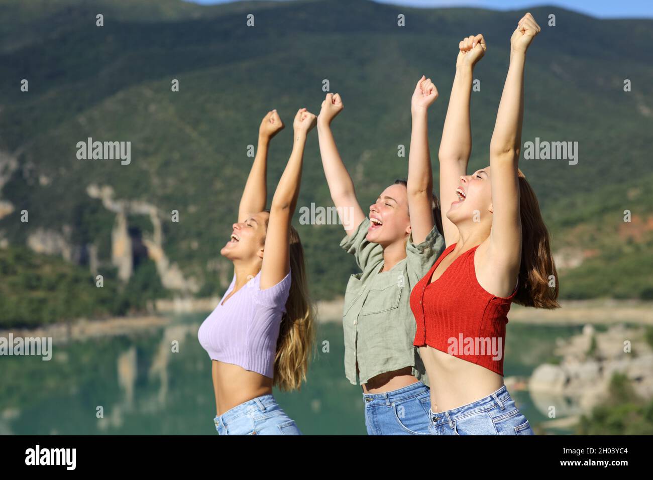 Three happy friends celebrating vacation raising arms in a mountain ...