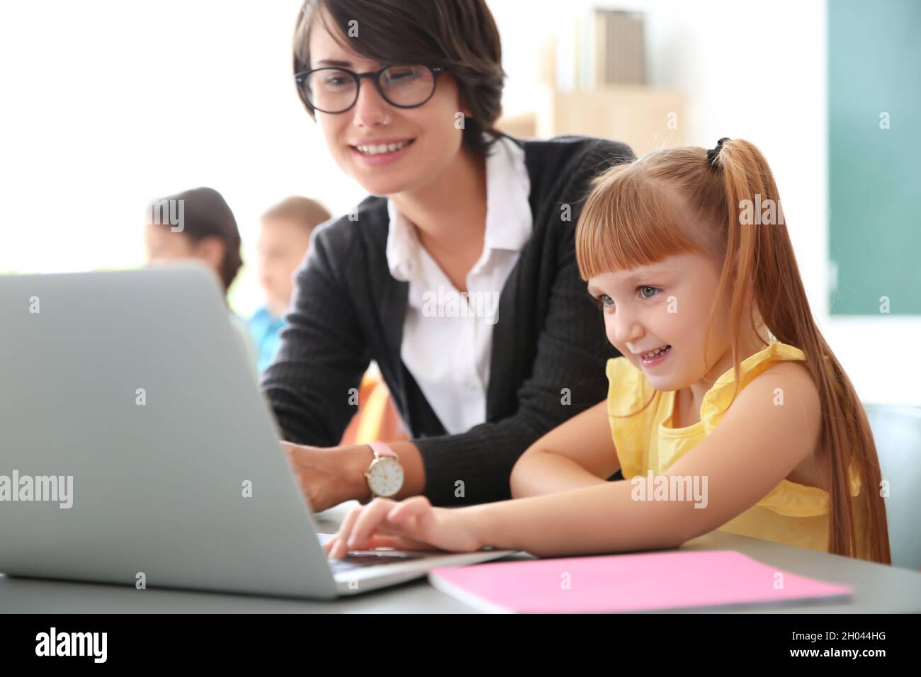 Female teacher helping child with assignment at school Stock Photo - Alamy