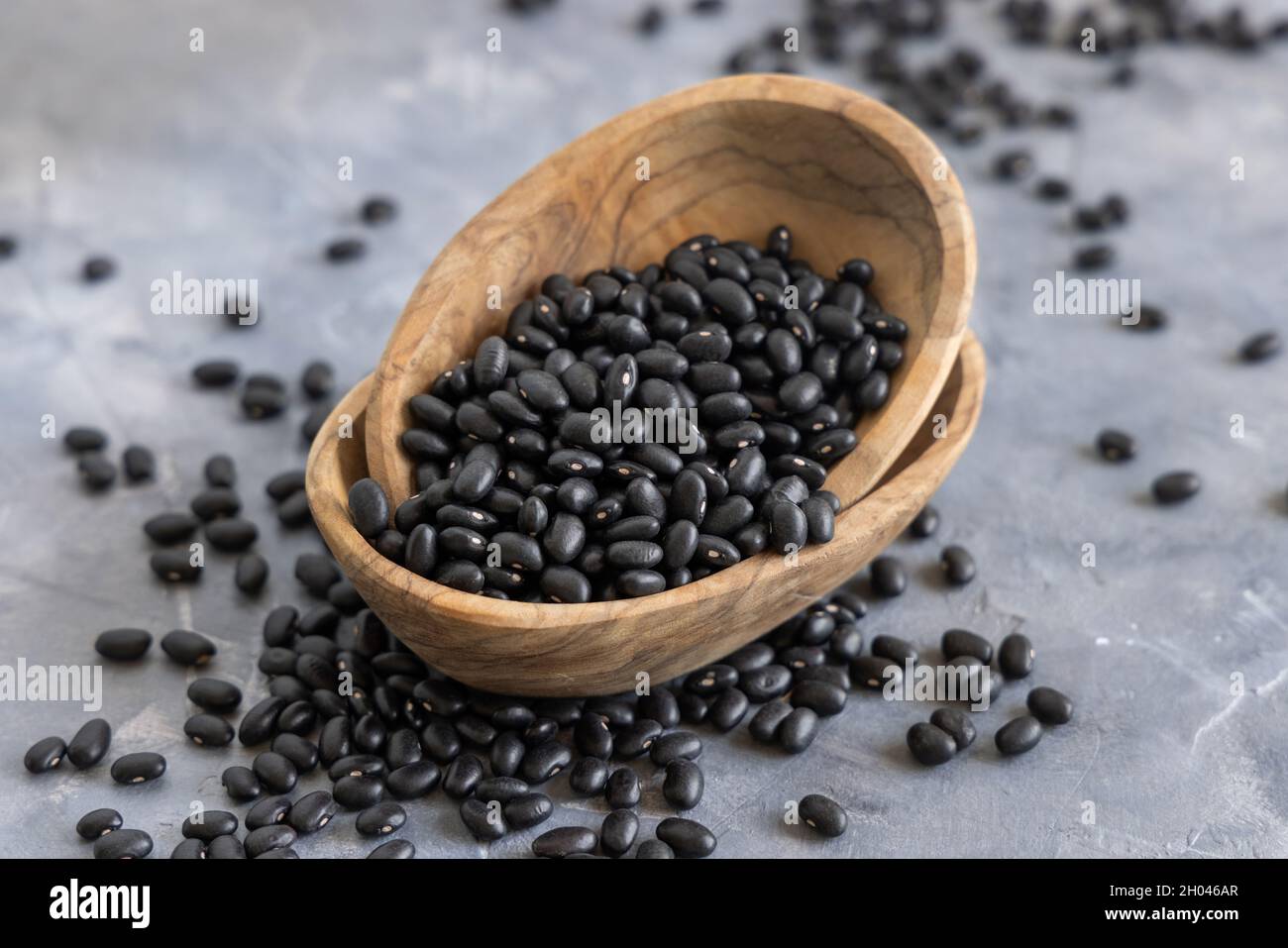 Wooden bowls full of dry black beans on grey table closeup. Healthy ...
