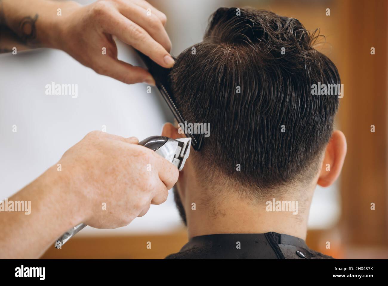 Close-up professional barber cuts the hair, beard of man at barbershop ...
