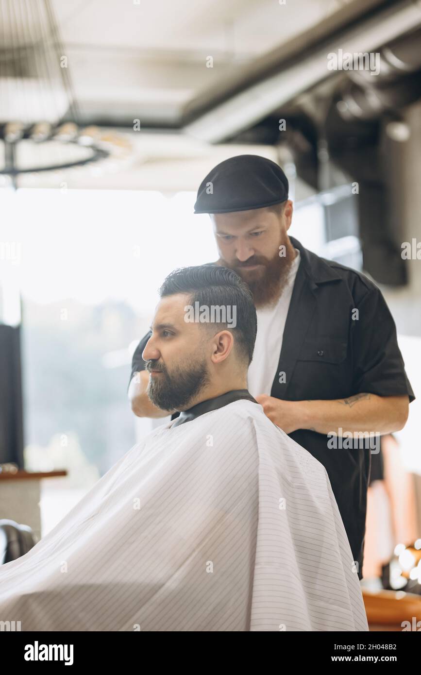 Two handsome men at barbershop. Stylish red-bearded barber and client ...