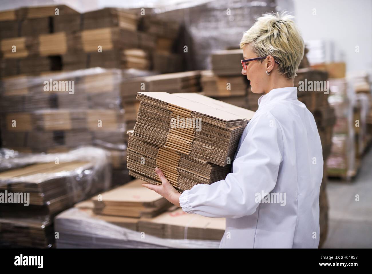 Woman carrying unmade cardboard boxes. Side view, warehouse interior ...