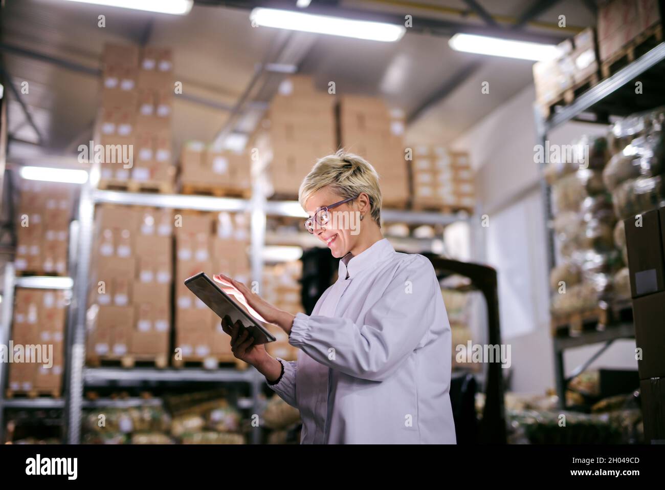 Happy Caucasian factory worker using tablet while standing in warehouse ...
