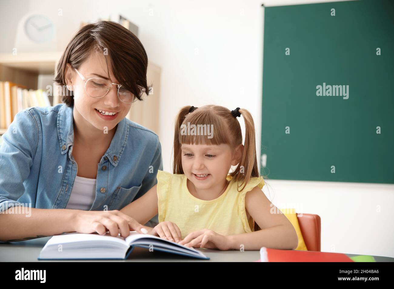 Female teacher helping child with assignment at school Stock Photo - Alamy