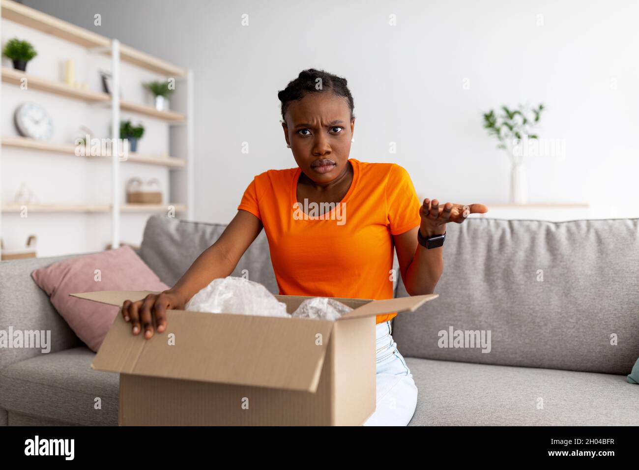 Wrong parcel. Confused black woman unpacking cardboard box ...