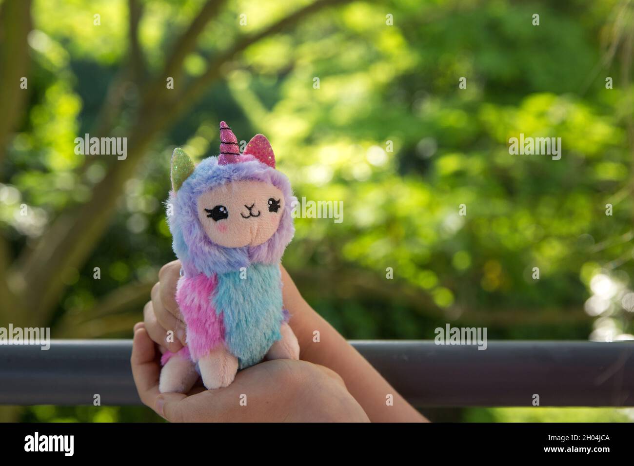 Colored plush llama unicorn in hands little girl with greens on background. Famous and popular kids toy Stock Photo Alamy