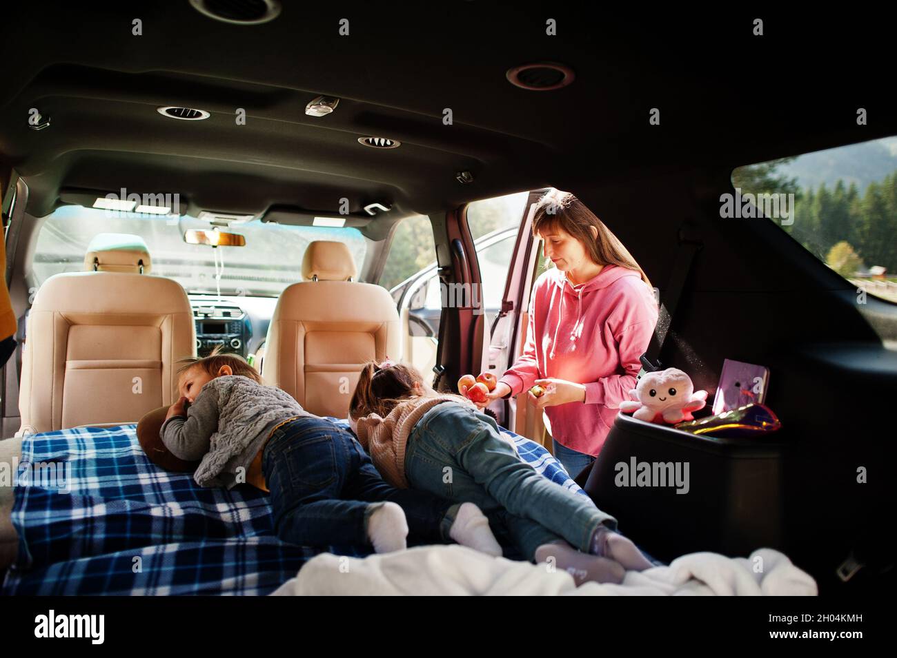 Mother with two daughter kids at vehicle interior. Children in trunk ...