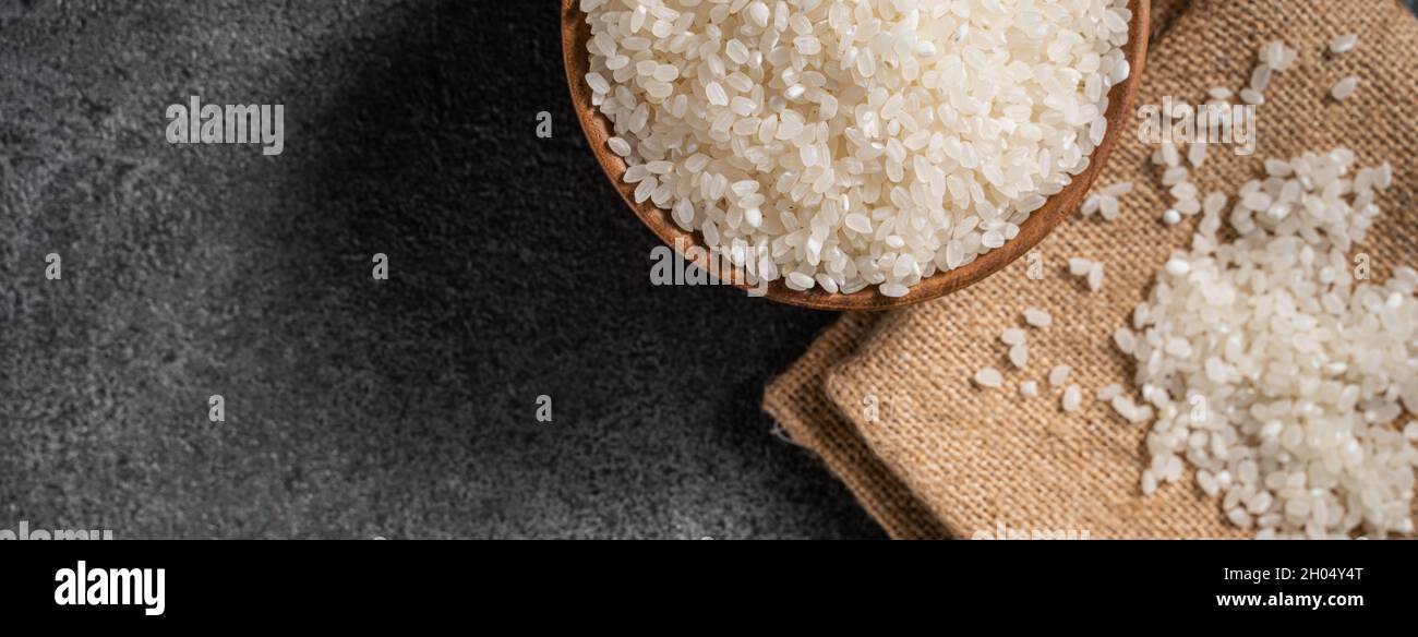 White raw rice in a bowl with the ear on the dark black table ...