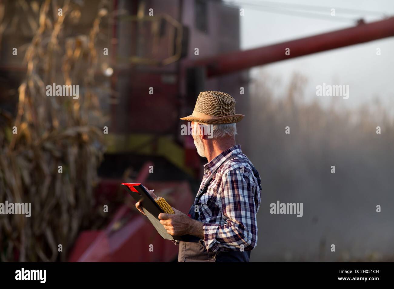 Senior man writing notes about yield in front of combine harvester in ...