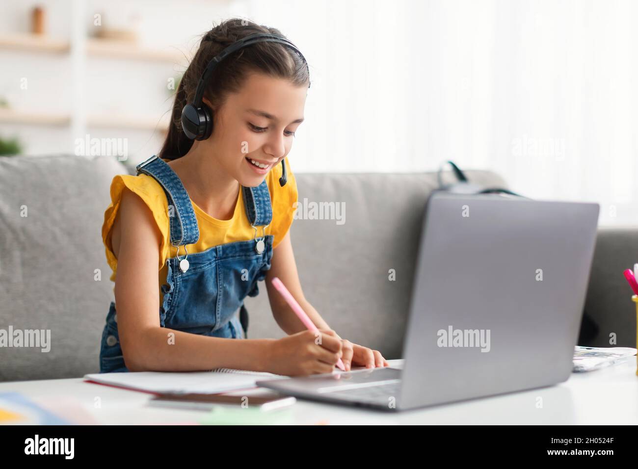 Studying At Home. Cheerful schoolgirl in headset sitting on couch at ...