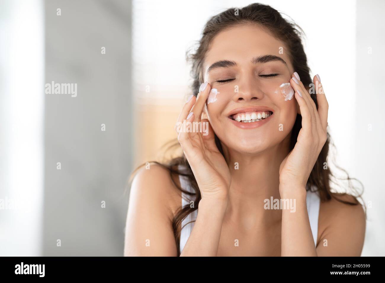 Headshot Of Pretty Lady Applying Facial Cream On Cheeks Smiling With