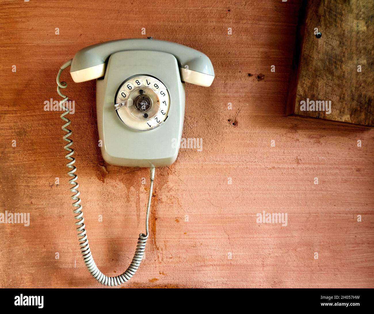 Light gray analog phone with cracked dial and dirty coiled cord hangs ...
