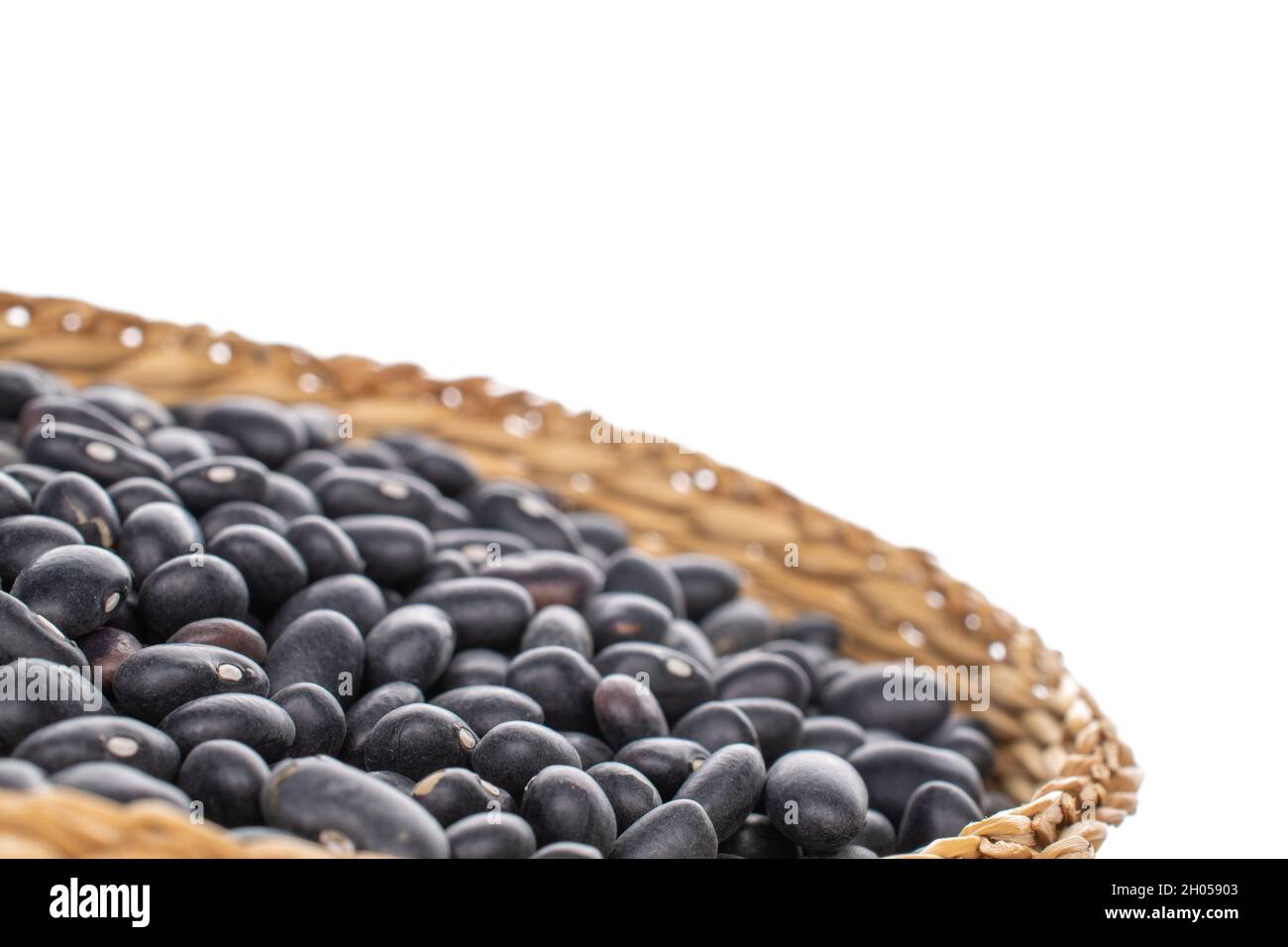 Uncooked organic, black dried beans in a straw plate, close-up ...