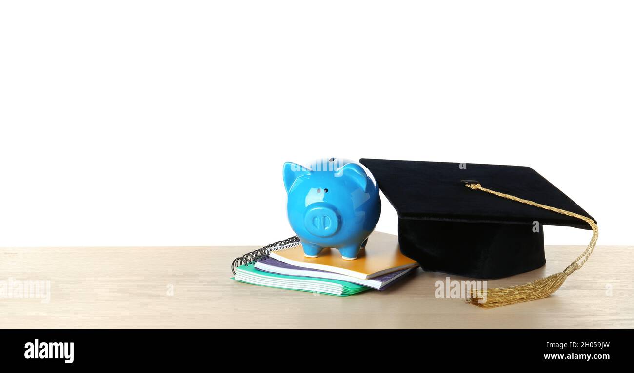 Graduation hat with piggy bank and notebooks on table against white ...