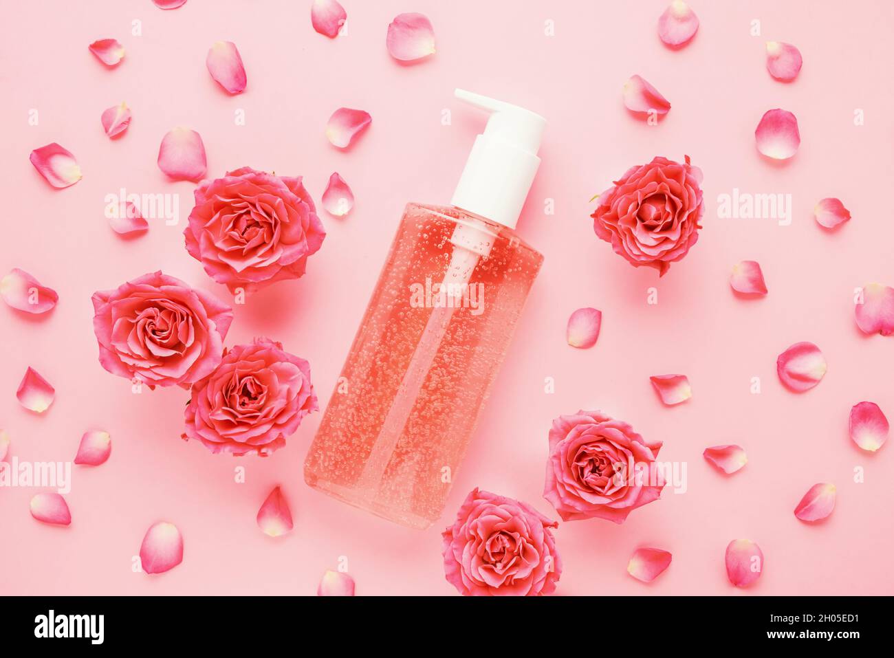 Dispenser bottle of pink shower gel or soap, and pink rose flowers on a ...