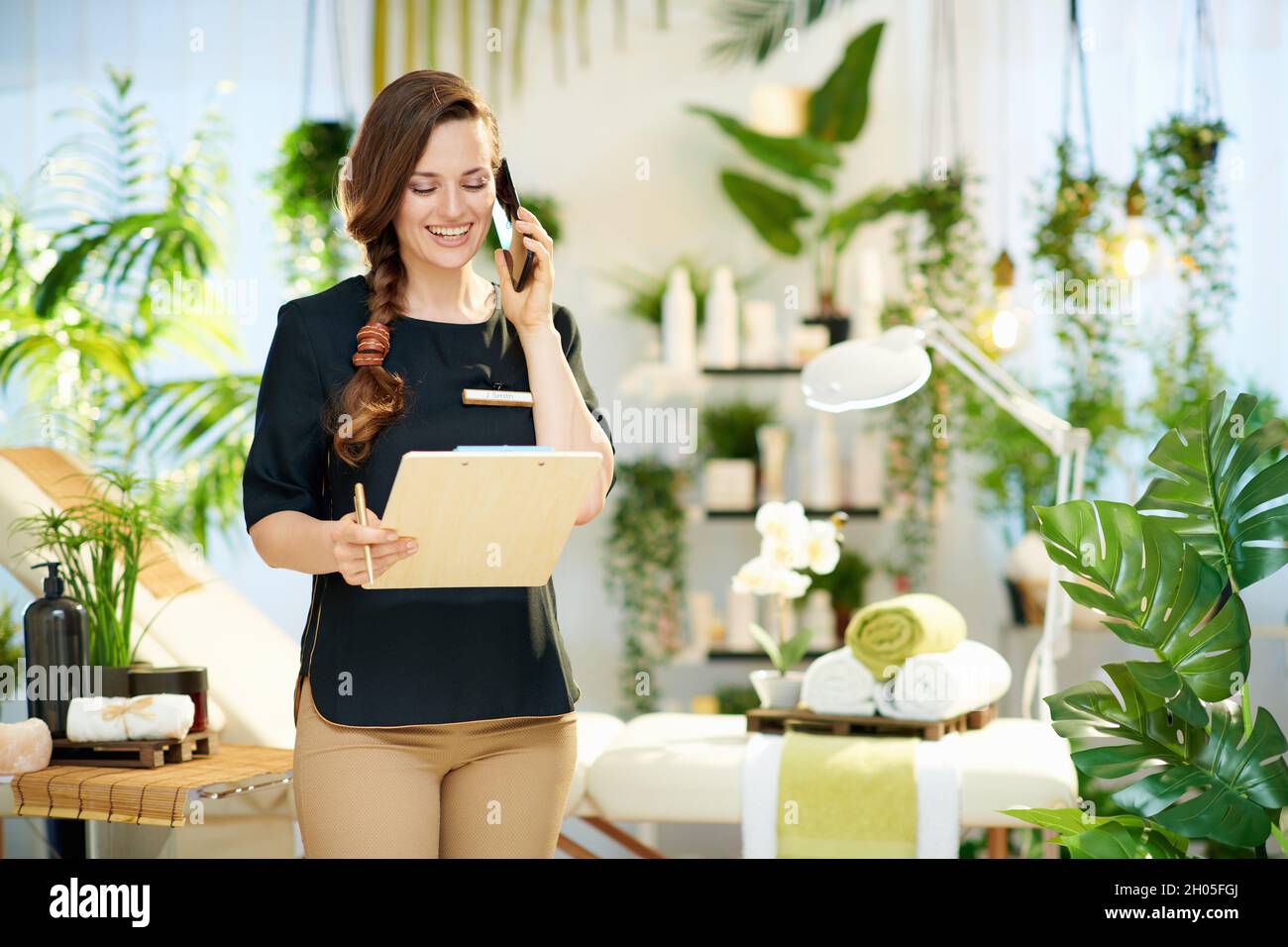 happy female worker with clipboard speaking on a smartphone in modern ...