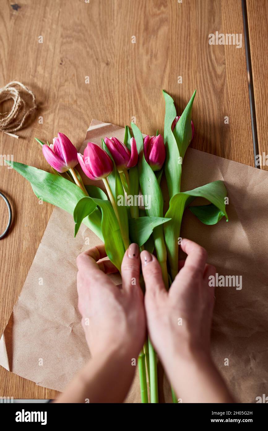 Female hands arranging pink tulips bouquet on wooden table, floristic ...