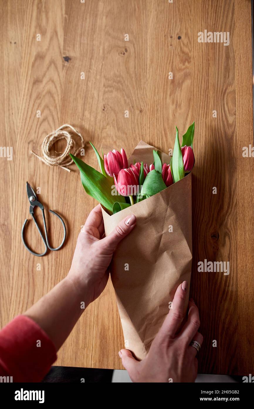 Female hands arranging pink tulips bouquet on wooden table, floristic ...