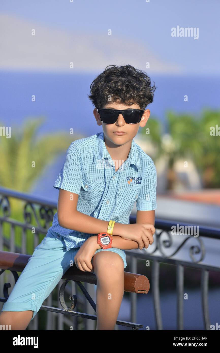 Portrait of a cool Armenian boy wearing sunglasses sitting on the fence ...