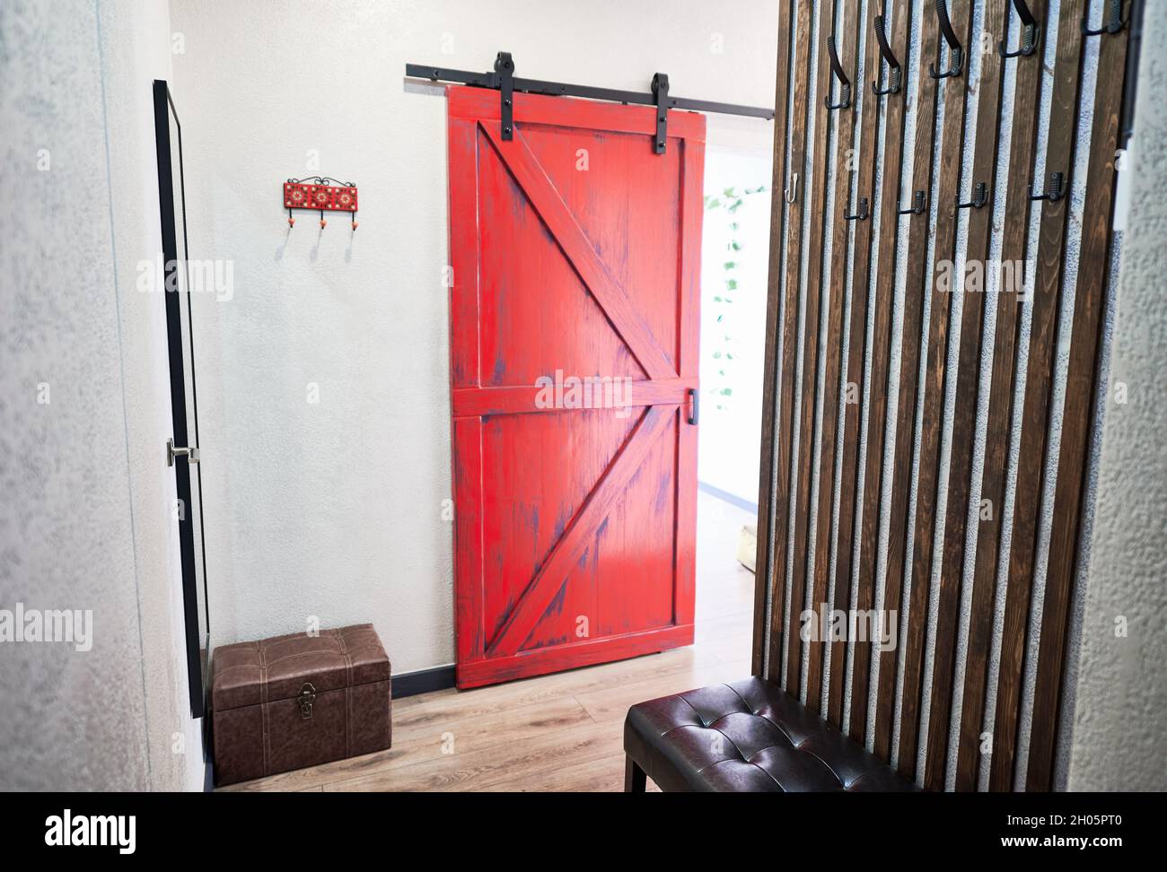 View of red door in corridor with big mirror on wall and ottoman ...