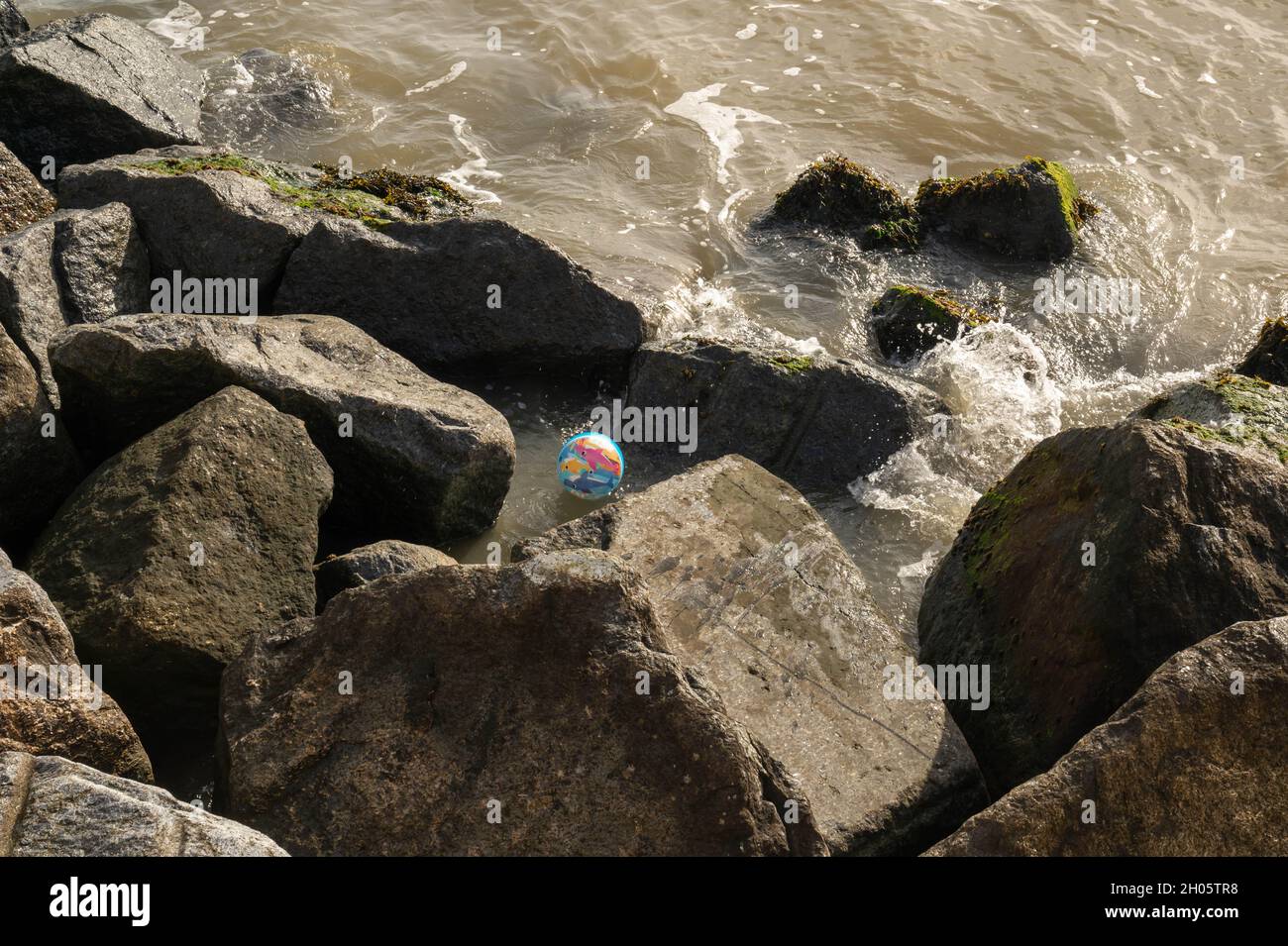 A lost colourful beach ball caught in the Sea defence rocks at ...