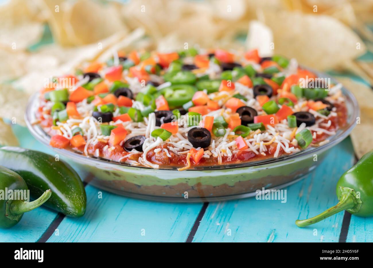 View of a homemade 7 layer dip ready for snacking, with chips in behind ...