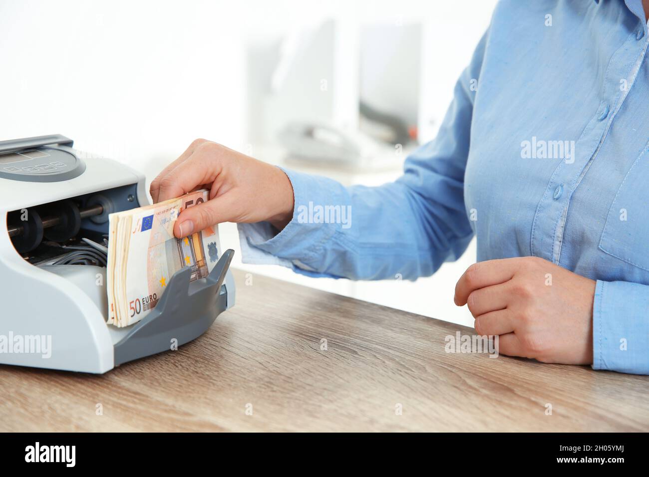 Female teller putting money into currency counting machine at cash ...