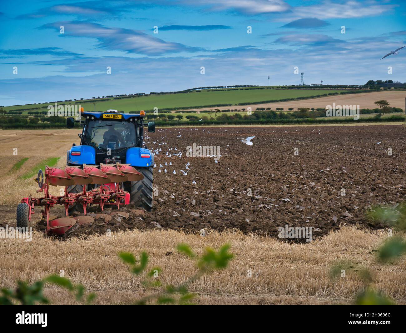 A farm tractor ploughing a field of stubble on a partly sunny day in ...