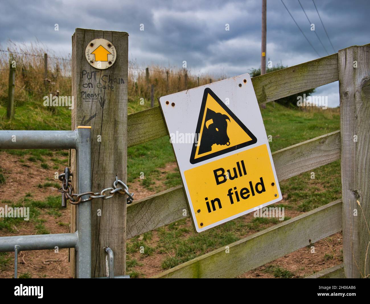 A yellow and black sign fixed to a wooden fence warns walkers of a bull ...