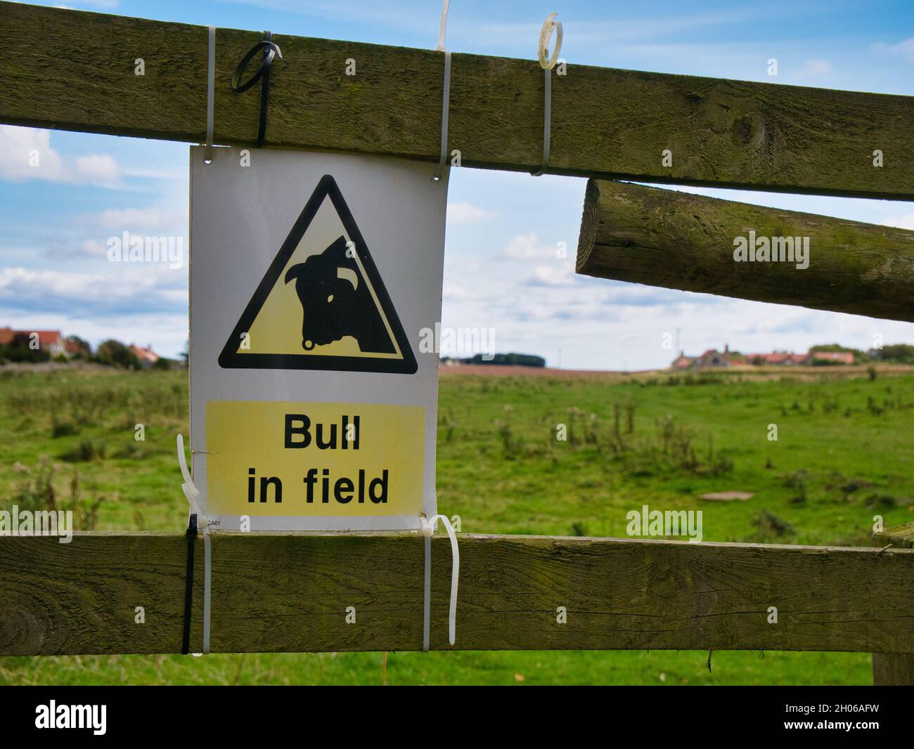 A yellow and black sign fixed to a wooden fence warns walkers of a bull ...