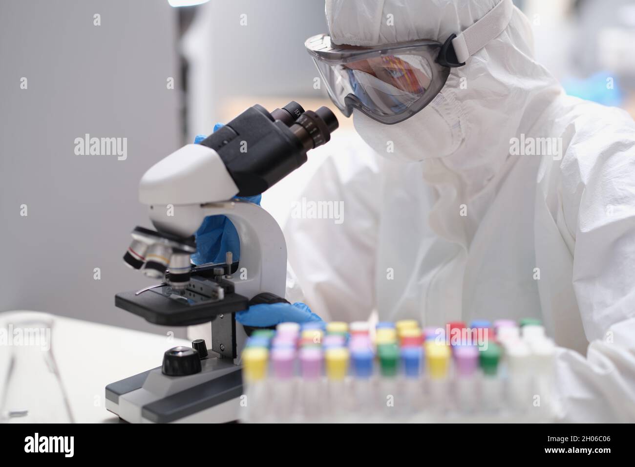 Scientist in protective suit and mask looks through microscope Stock ...