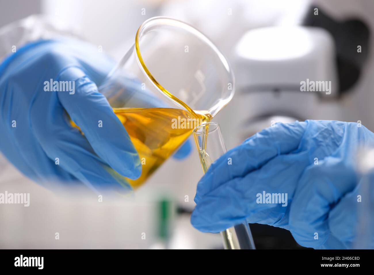 Gloved scientist pours yellow oily liquid from flask into test tube ...