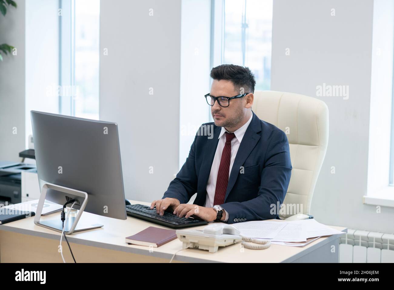 Busy director in elegant suit typing and looking at computer screen ...