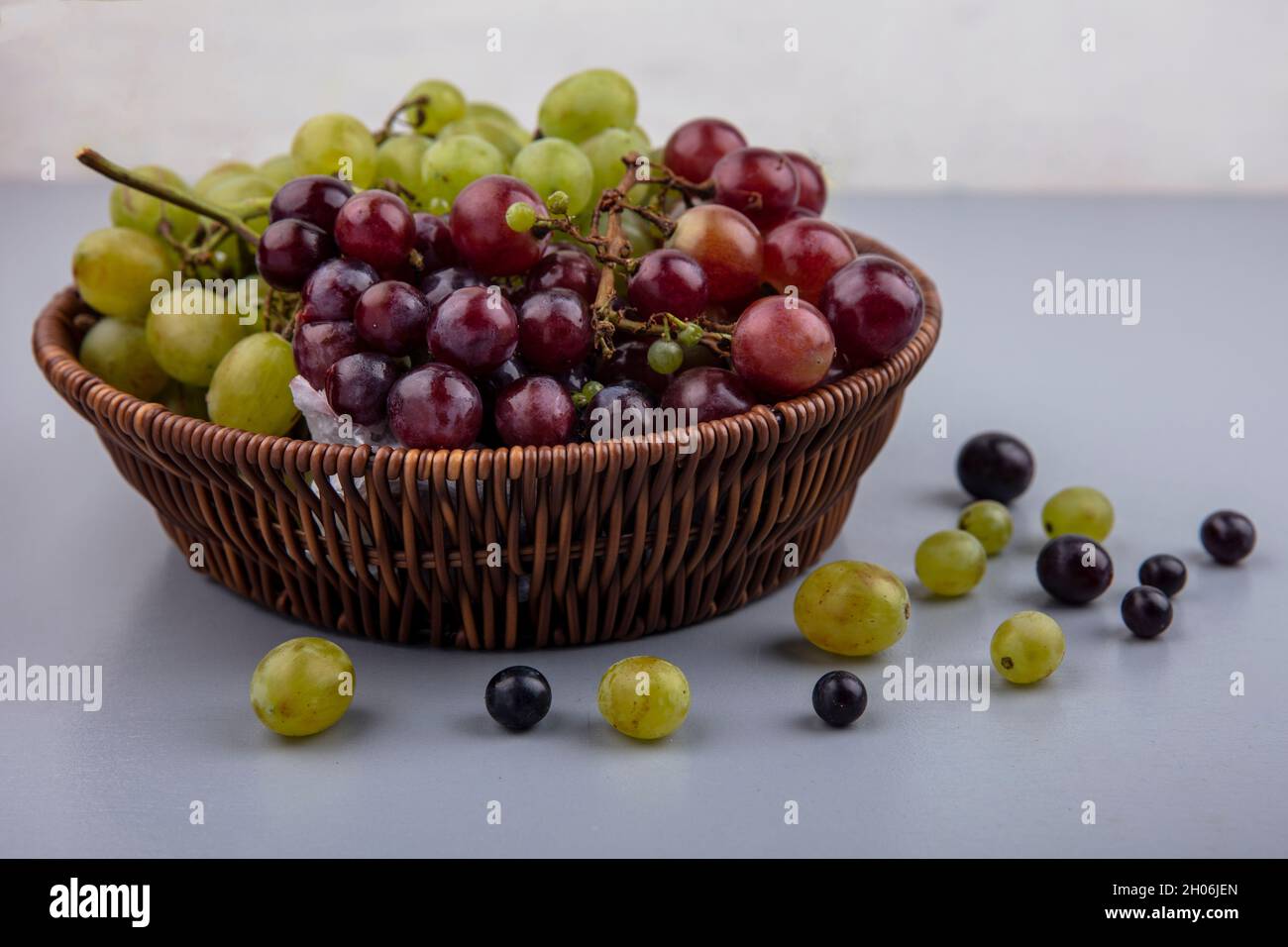 side view of basket of grapes and grape berries on gray surface and ...