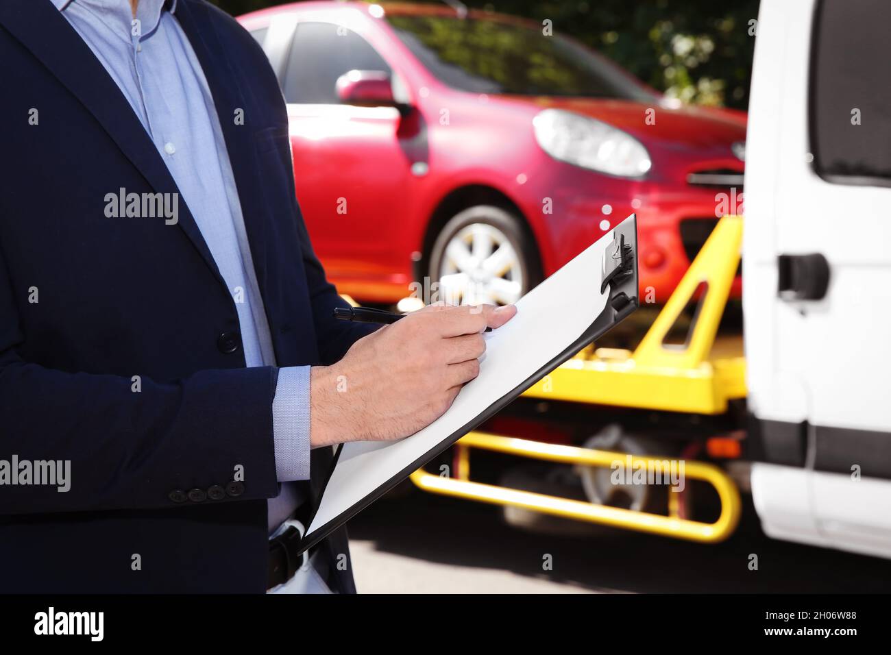 Man with clipboard near tow truck and broken car outdoors, closeup ...
