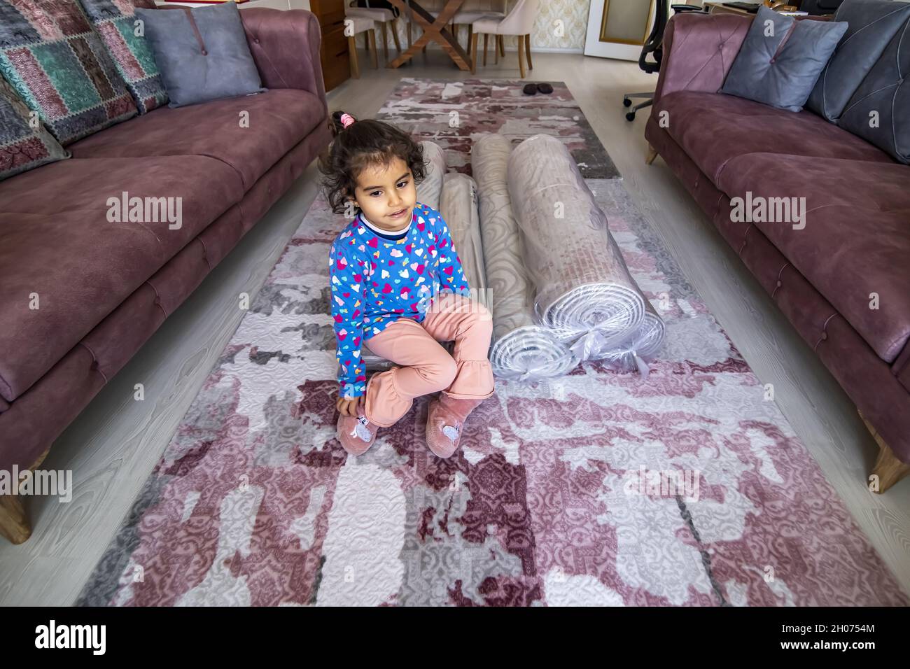 Sweet girl sitting on rolled up carpets after washing in the living ...