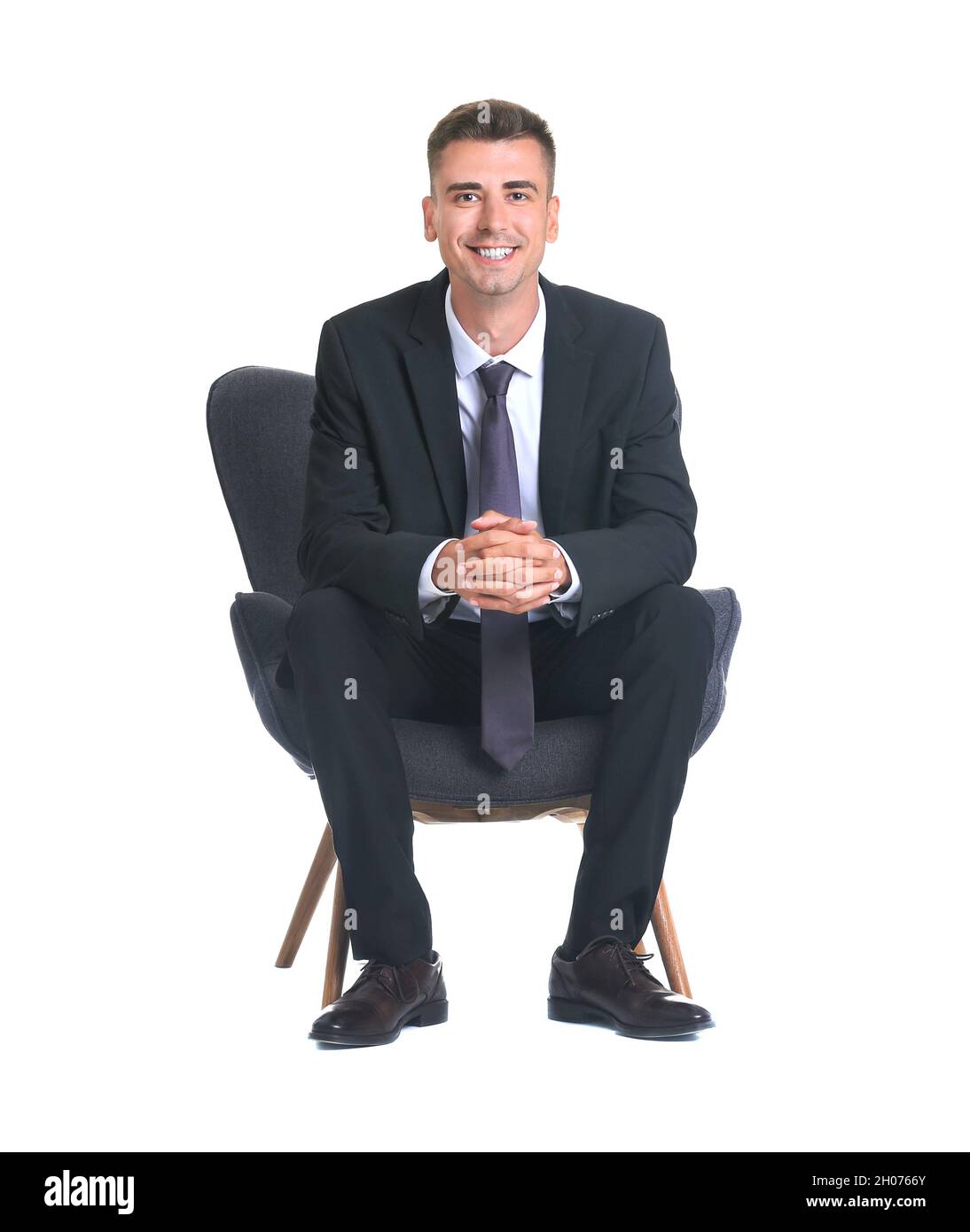 Handsome young man in suit sitting in armchair on white background ...
