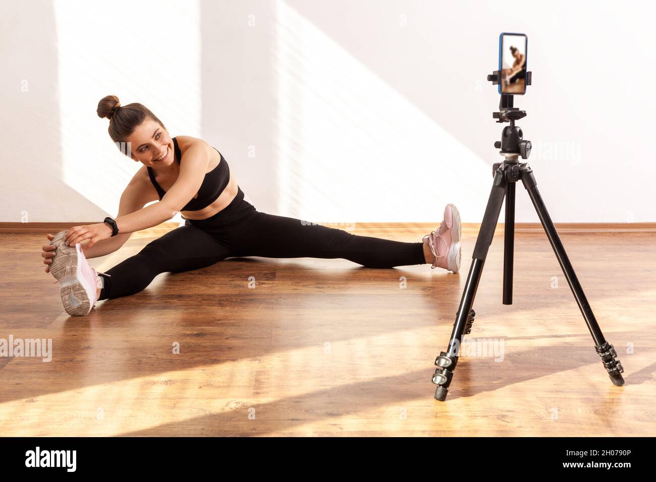 Girl coach stretching legs, broadcasting online class, using phone on ...