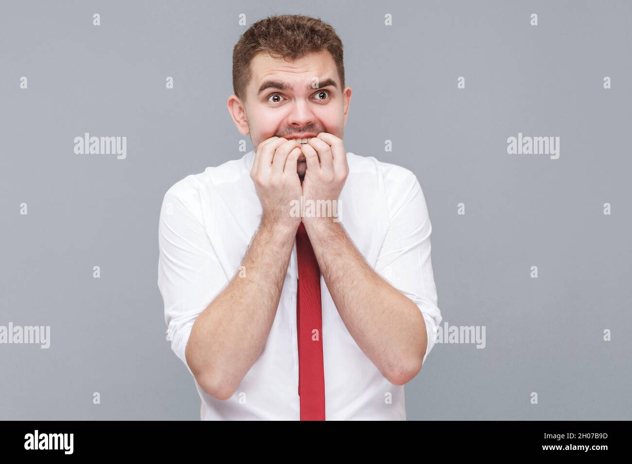 Portrait of young nervous man in white shirt and tie standing, bitting ...
