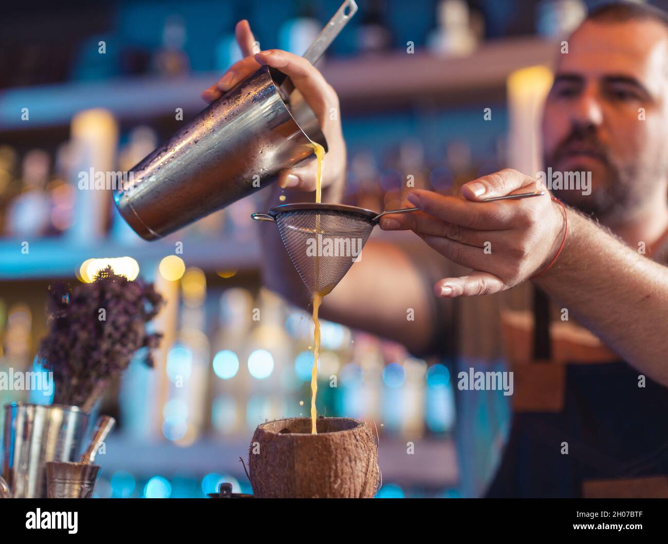Bartender pouring juice using strainer in coconut shell in bar Stock ...