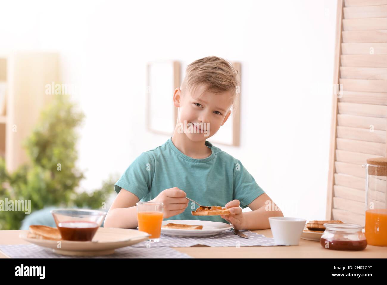Cute little boy spreading jam onto tasty toasted bread at table Stock ...