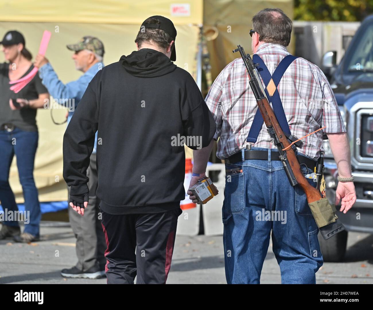 A man wears a long gun on his back and carries bullets while attending ...