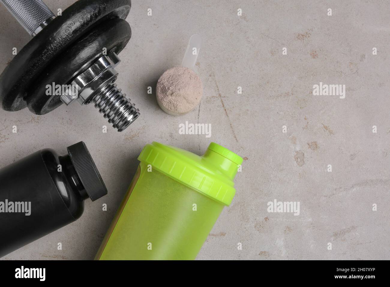 Bottle with protein shake, scoop of powder and dumbbell on grey ...