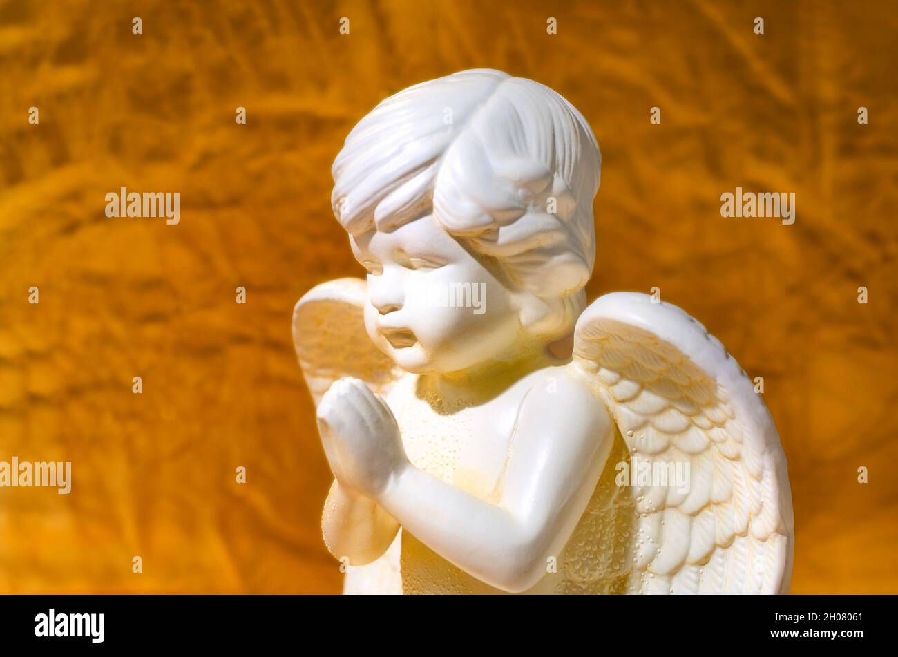 White angel boy sculpture near the firelight with golden shadows on the ...