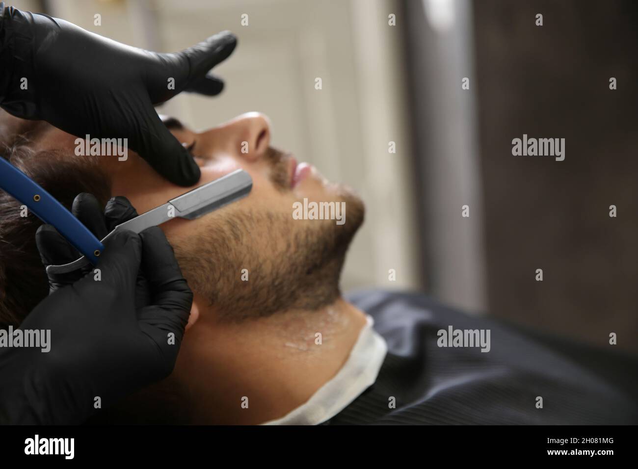 Professional hairdresser shaving client with straight razor in ...