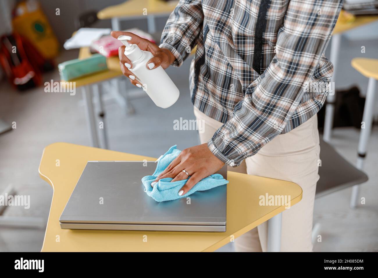 Young female teacher using spray to disinfect desks in classroom Stock ...